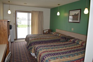 Quarto de hotel com duas camas, uma escrivaninha, uma cadeira e vista para o exterior através de uma porta de correr.