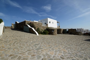 Pátio com piso de pedra, um edifício branco com fachada de pedra e cerca branca.