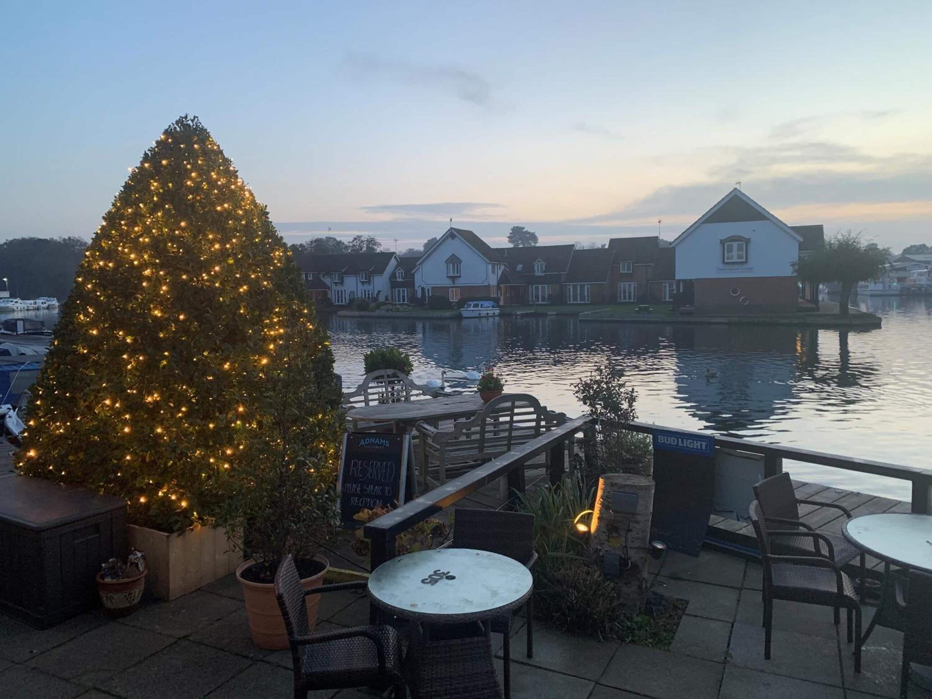 Um restaurante à beira-mar com uma árvore de Natal, mesas ao ar livre e vista para as casas do outro lado da água.