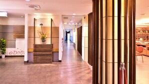 Um hall de hotel com um corredor comprido, uma mesa de recepção e uma escadaria.