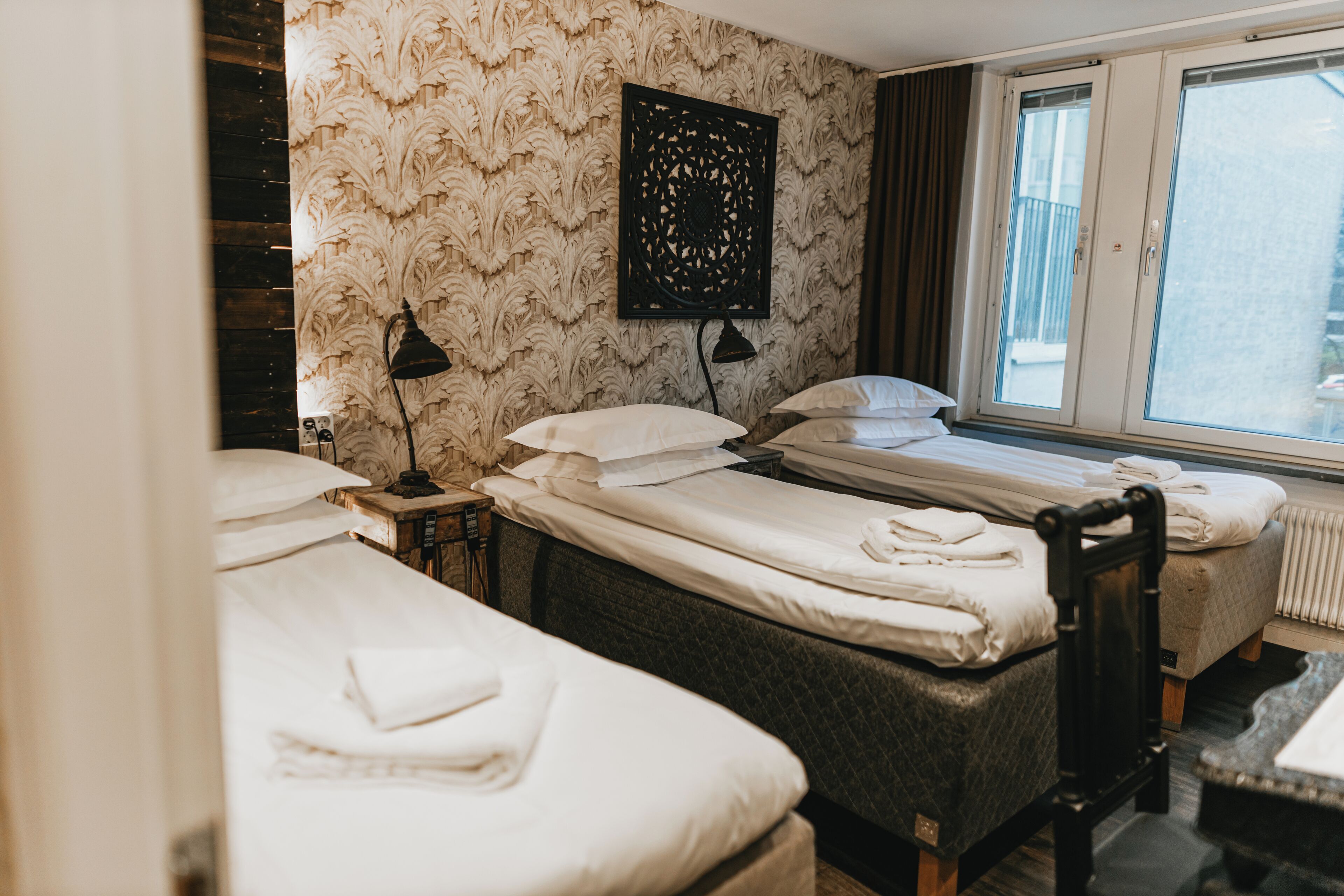 Quarto de hotel com duas camas, um radiador, uma janela com cortinas e um painel decorativo na parede.