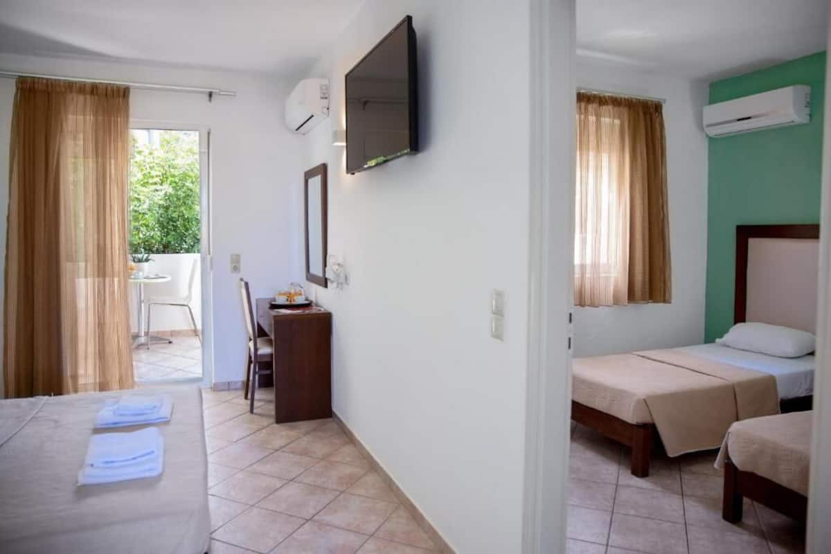Quarto com duas camas, uma escrivaninha, uma cadeira e uma televisão fixada na parede.