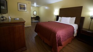 Quarto de hotel com cama de madeira, escrivaninha com telefone, cadeira e luminária de mesa.