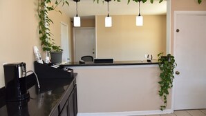 Uma área de recepção com balcão preto, máquina de café, planta em vaso e luminárias pendentes.