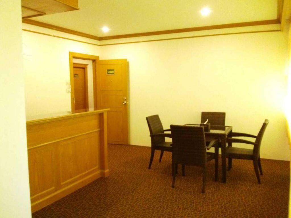 Quarto de hotel com balcão de atendimento de madeira, uma porta fechada e uma pequena mesa de jantar com quatro cadeiras.