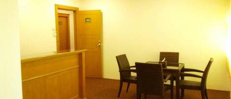 Quarto de hotel com balcão de atendimento de madeira, uma porta fechada e uma pequena mesa de jantar com quatro cadeiras.