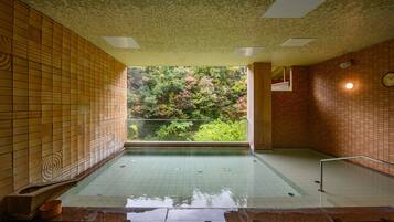 Área de spa com piso ladrilhado, bacia de pedra e vista para uma floresta através de uma divisória de vidro.