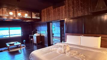 Quarto com uma cama grande, uma escrivaninha e uma cadeira. Janelas oferecem vista para o oceano.