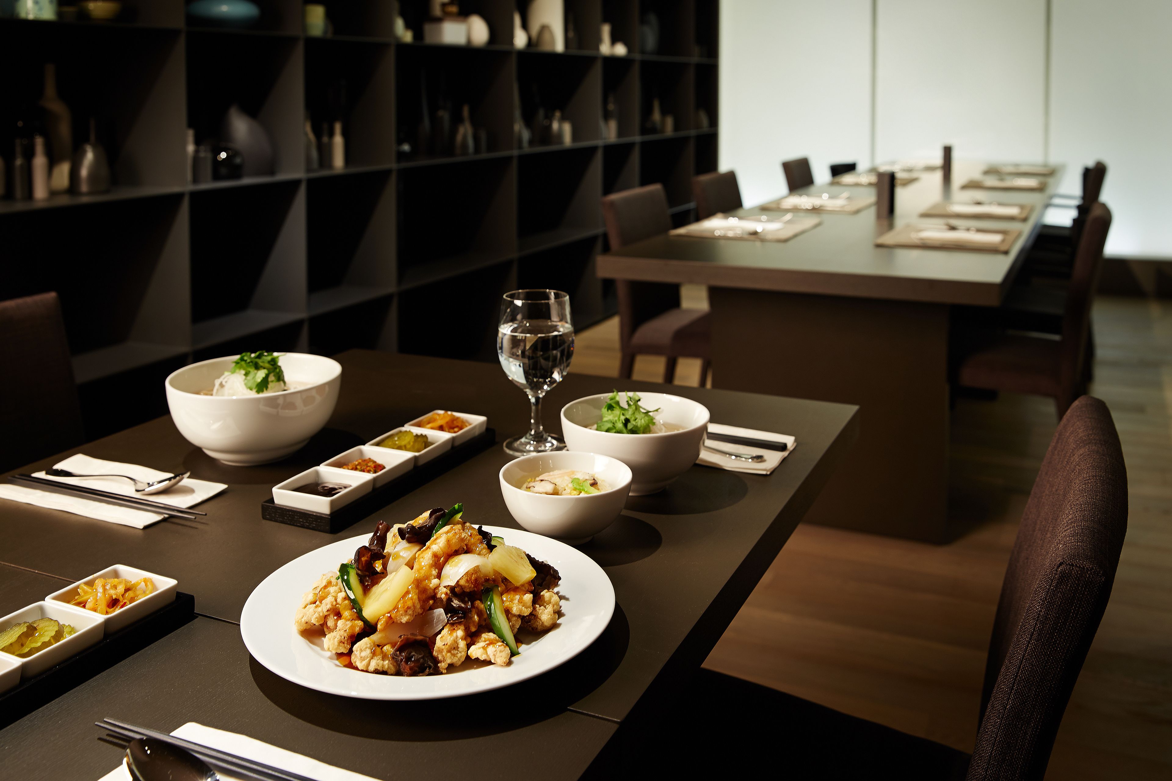 Uma mesa de jantar posta com diversos pratos, incluindo uma salada em uma tigela, um prato de legumes salteados e um copo de água.