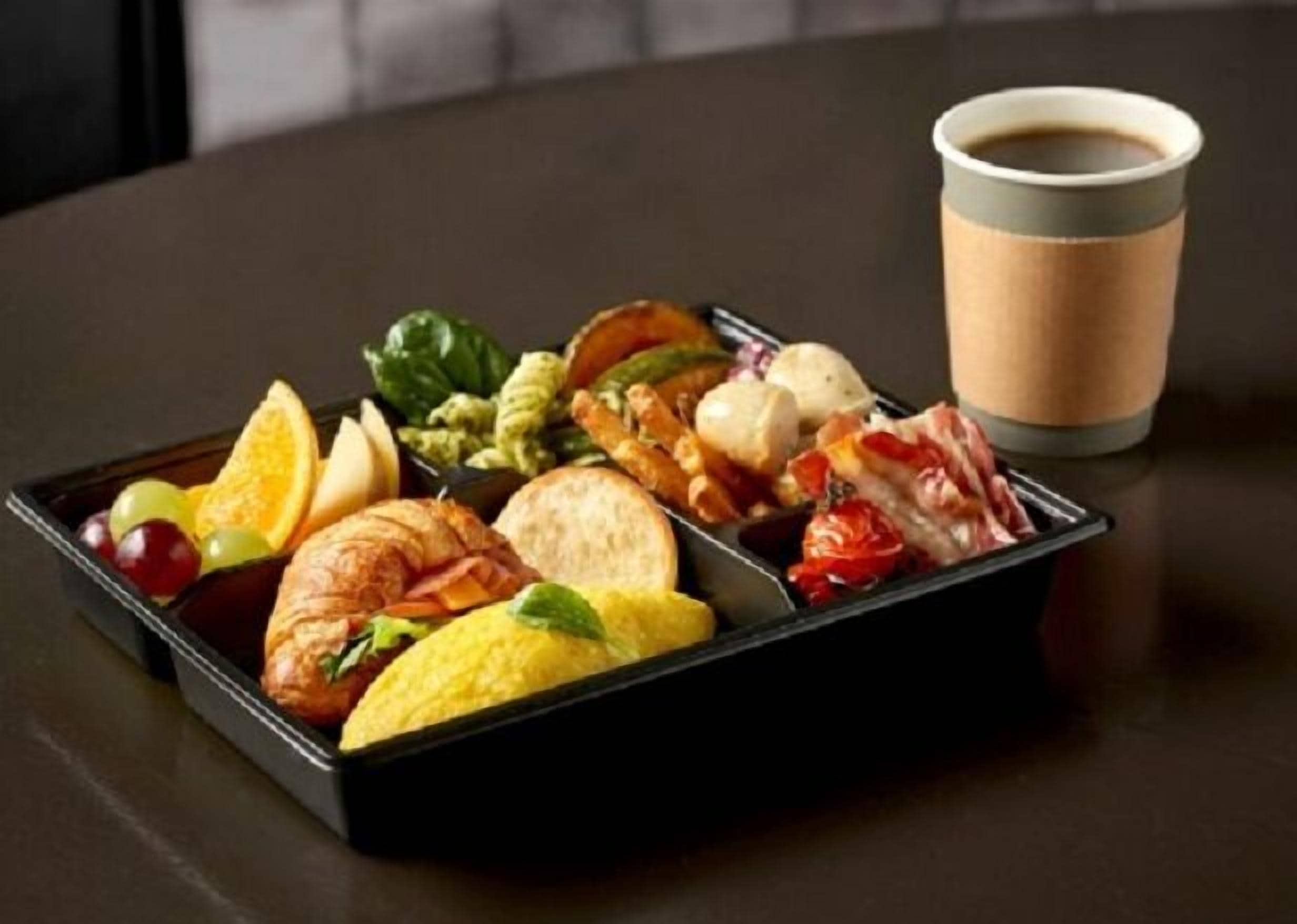 Uma bandeja de refeição com diversos alimentos e uma xícara de café sobre uma mesa.