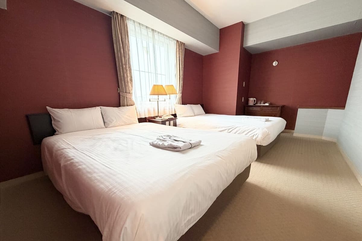 Quarto de hotel com duas camas, mesa de cabeceira, abajur e uma pequena mesa com uma xícara.