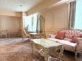 Quarto com um sofá rosa, uma mesa de centro de vidro, uma cadeira e um espelho.