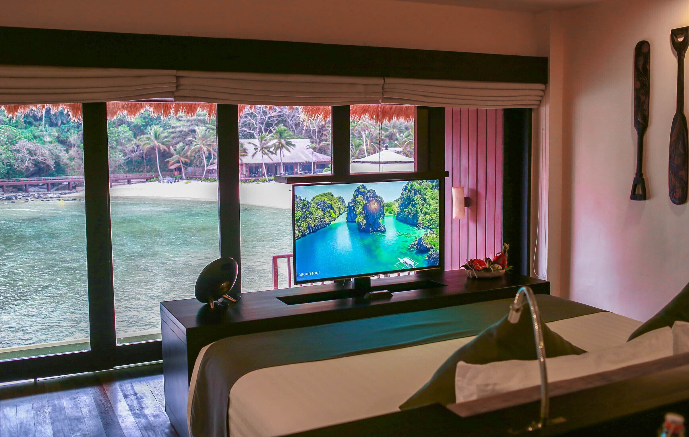 Quarto de hotel com uma janela grande que oferece vista para uma praia e palmeiras.