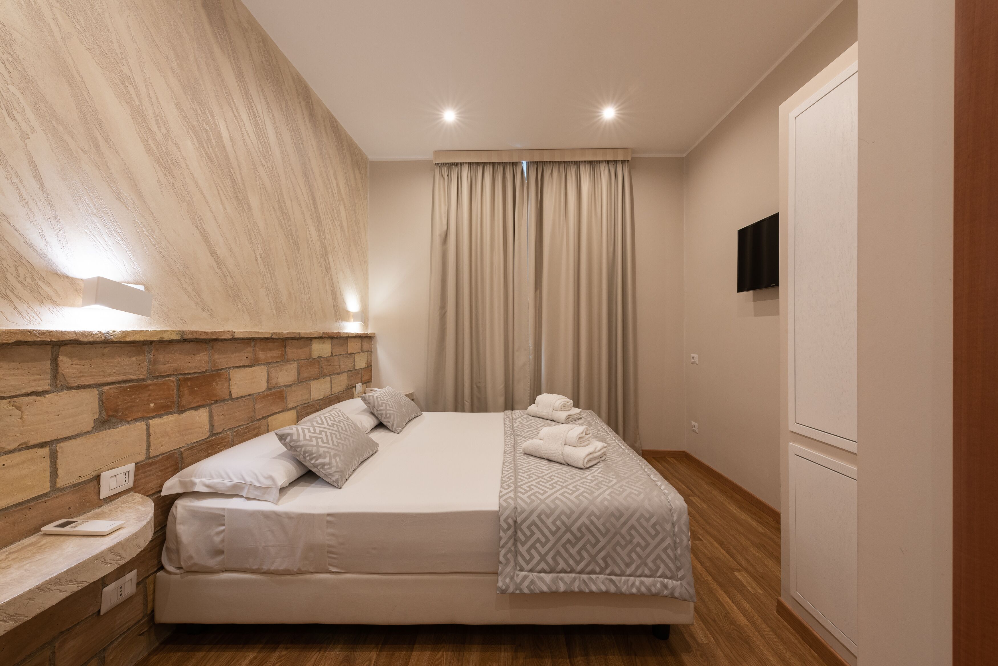 Quarto bem arrumado com parede de tijolos, cama com travesseiros e manta, televisão de tela plana e piso de madeira.