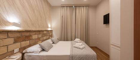Quarto bem arrumado com parede de tijolos, cama com travesseiros e manta, televisão de tela plana e piso de madeira.