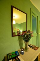 Um banheiro com parede verde, um espelho, um vaso com flores, uma caixa de lenços e um controle remoto em uma bancada.