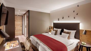 Quarto de hotel com uma cama grande, uma TV de tela plana, um painel de cabeceira de madeira e uma parede com letras iluminadas que formam a palavra 'Zzz'.
