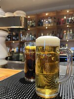 Um balcão de bar com um copo de chopp e um copo de cerveja em um apoio de bar preto.