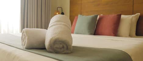 Cama bem arrumada com colcha verde, cabeceira de madeira e várias almofadas em cores diferentes.