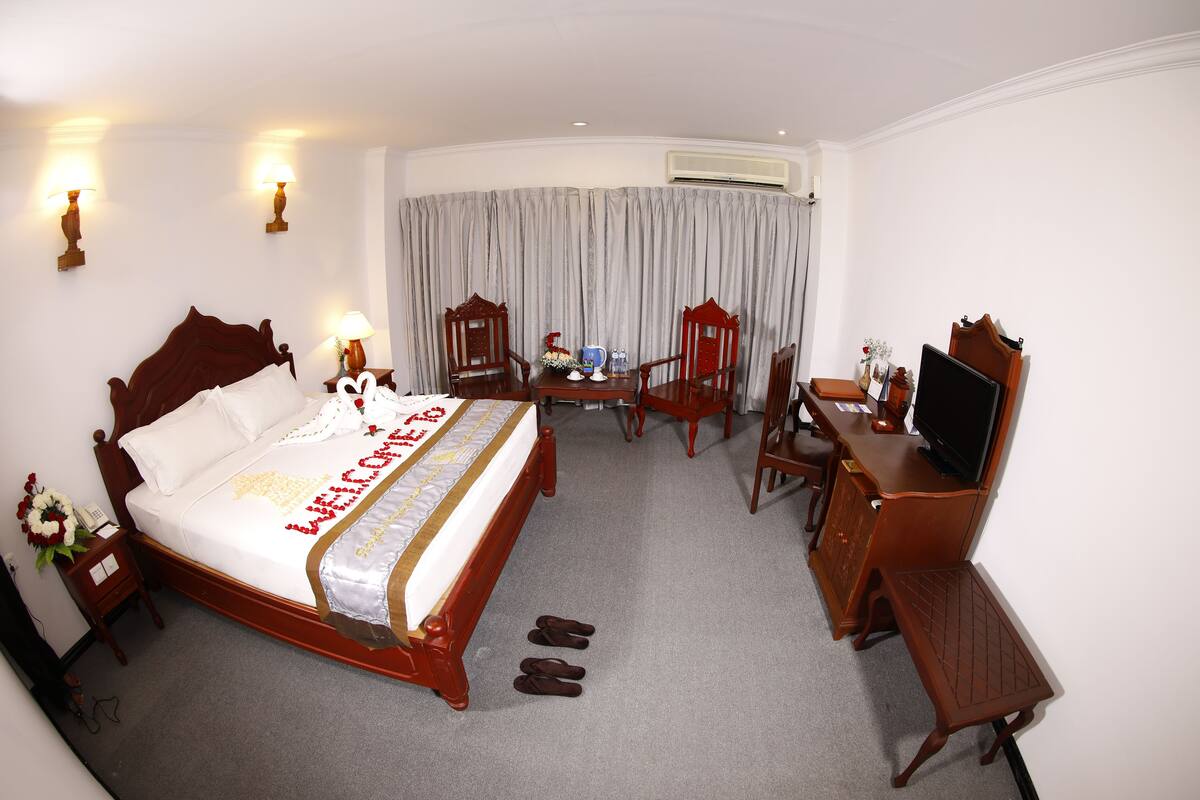 Quarto de hotel com uma cama grande, uma escrivaninha com televisão, uma cadeira e uma pequena mesa.
