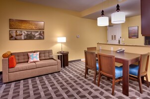 Quarto de hotel com sofá, mesa de jantar com cadeiras, luminária e obras de arte nas paredes.