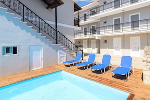 Uma área de piscina com espreguiçadeiras azuis, um deck de madeira e uma escadaria que leva a uma varanda.