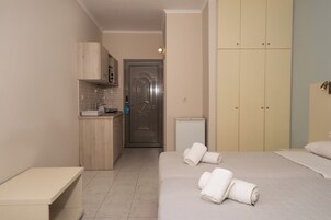 Quarto de hotel com cama, uma pequena mesa de cabeceira, armário e cozinha compacta.