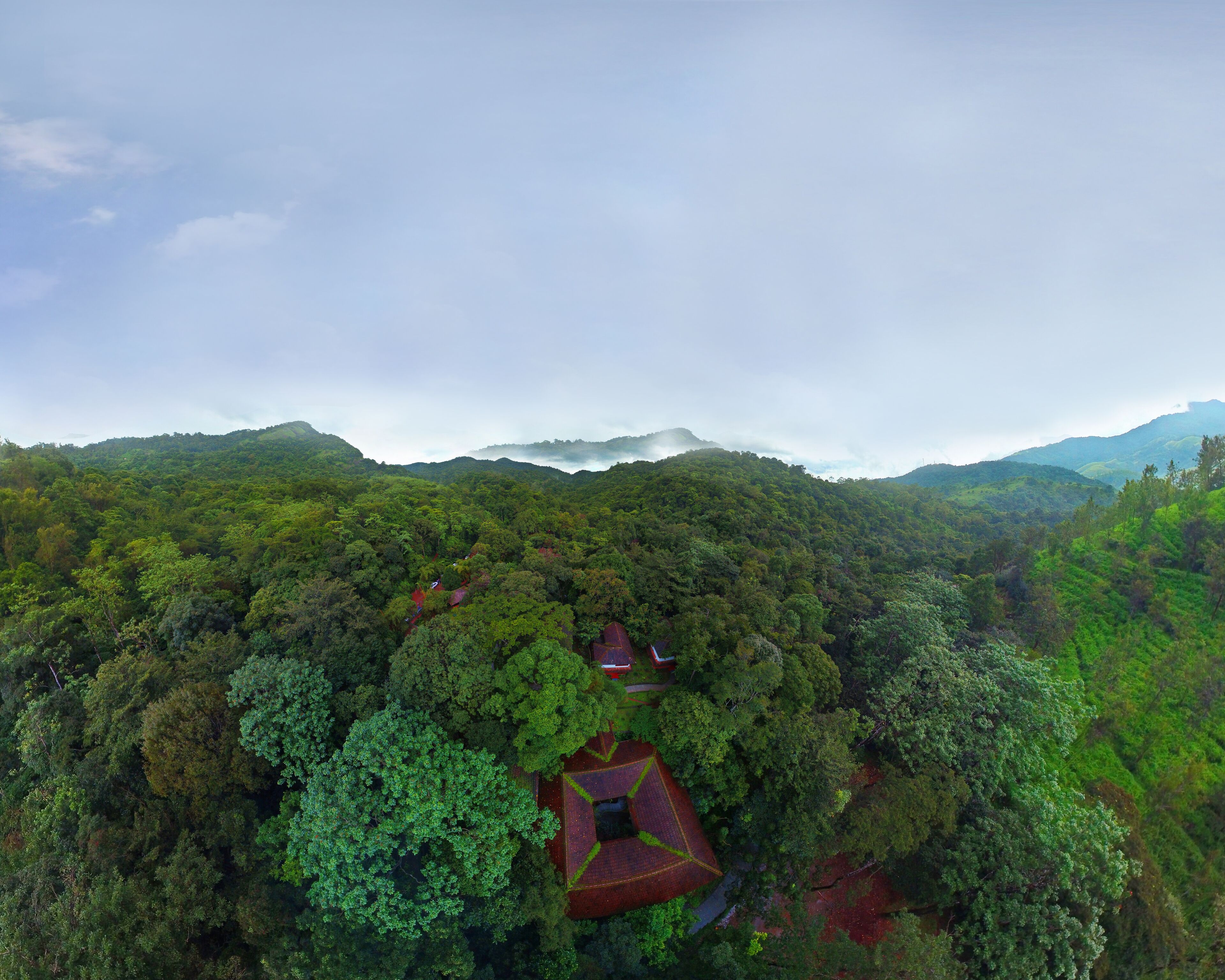 Vista aérea de uma área arborizada com um pequeno edifício rodeado por árvores densas.