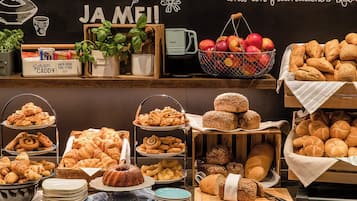 Vitrine de padaria com diversos produtos de panificação, incluindo pão, doces e uma cesta de maçãs.