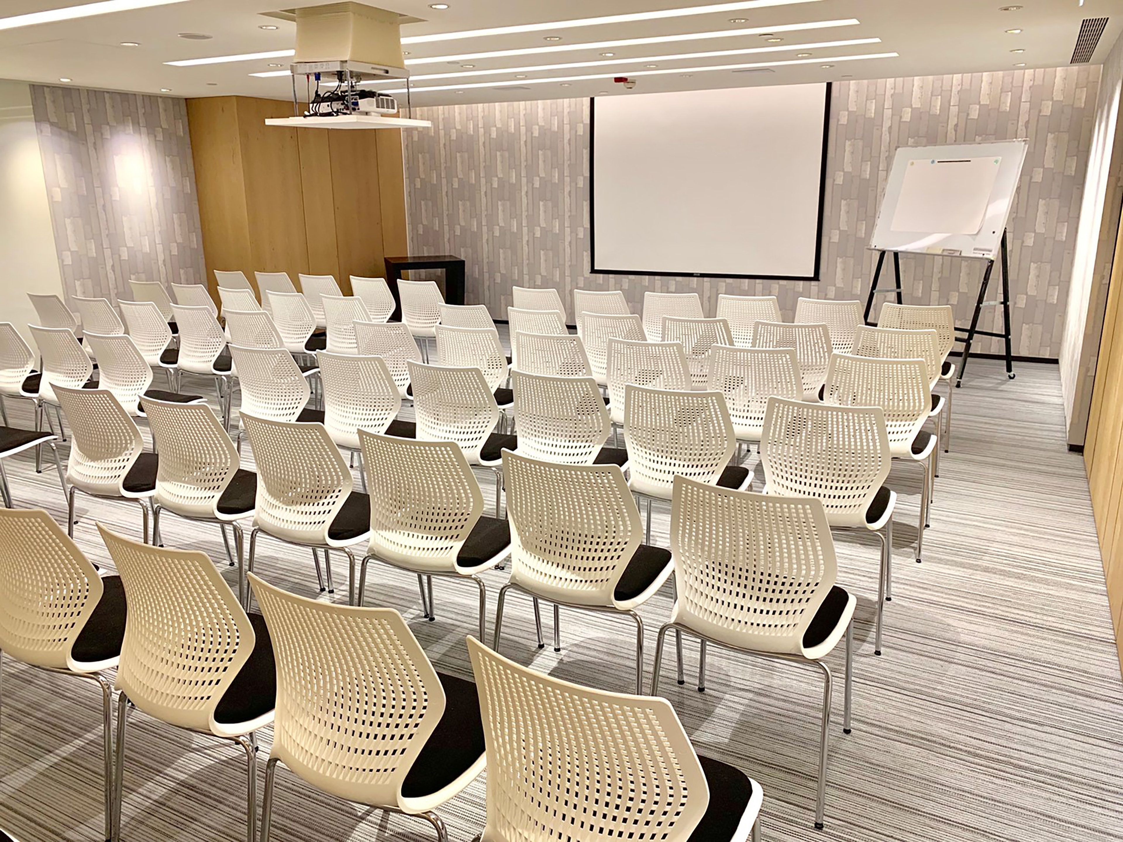 Uma sala de conferências com fileiras de cadeiras, uma tela de projetor e um quadro branco.