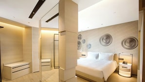 Quarto de hotel moderno com uma cama grande, mesas de cabeceira, espelho e arte decorativa na parede.