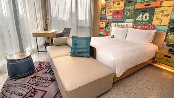 Quarto de hotel com cama, sofá, escrivaninha e uma janela grande.