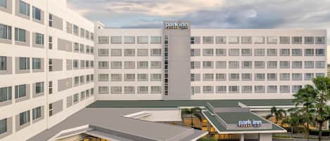 Um hotel moderno com uma torre central, vários andares e área de estacionamento.