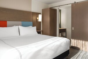 Quarto de hotel com uma cama grande, um guarda-roupa, um espelho e uma mesinha de cabeceira.