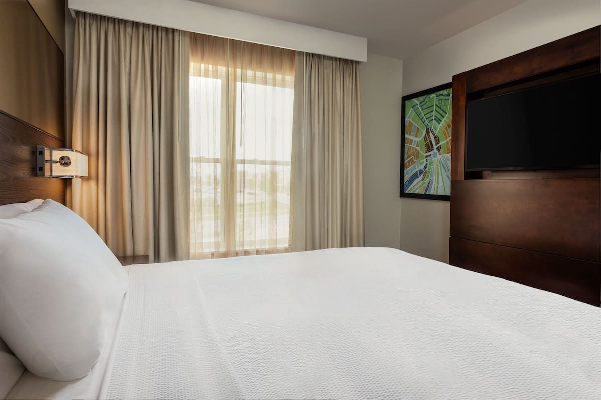 Quarto de hotel com uma cama grande, televisão de tela plana, cabeceira de madeira e janela com cortinas.