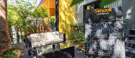 Café com um quadro negro exibindo promoções especiais e um sofá na área externa.