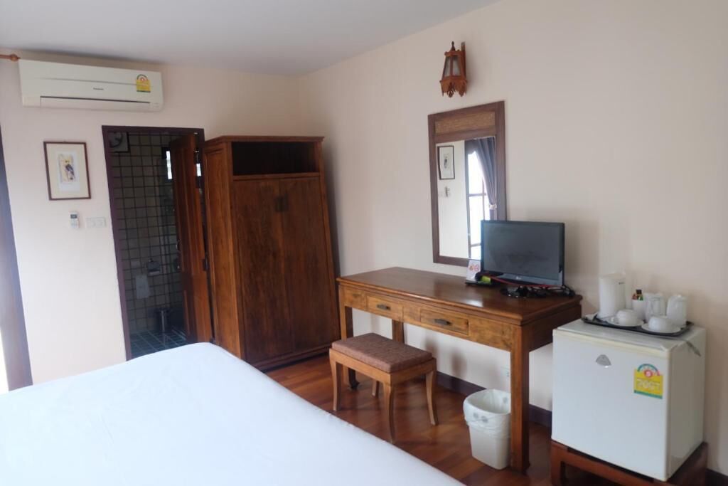Quarto com cama, escrivaninha de madeira, televisão, um pequeno frigorífico e guarda-roupa de madeira.