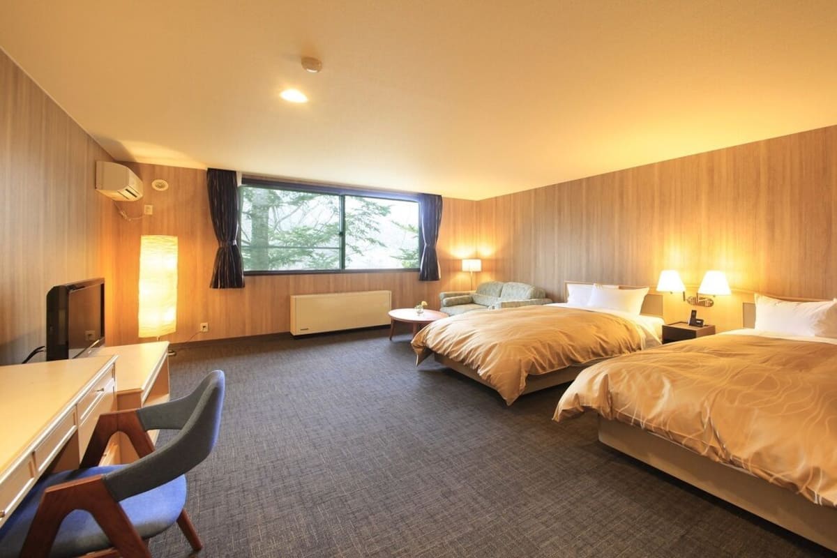 Quarto de hotel com duas camas, uma escrivaninha, uma cadeira, uma televisão e uma janela com cortinas.