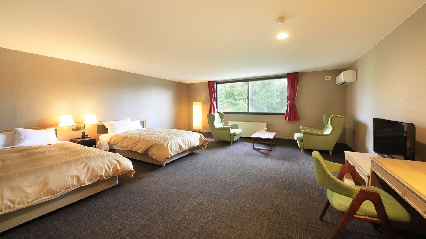 Quarto de hotel com duas camas, uma mesa, uma cadeira, uma televisão e uma janela com cortinas.