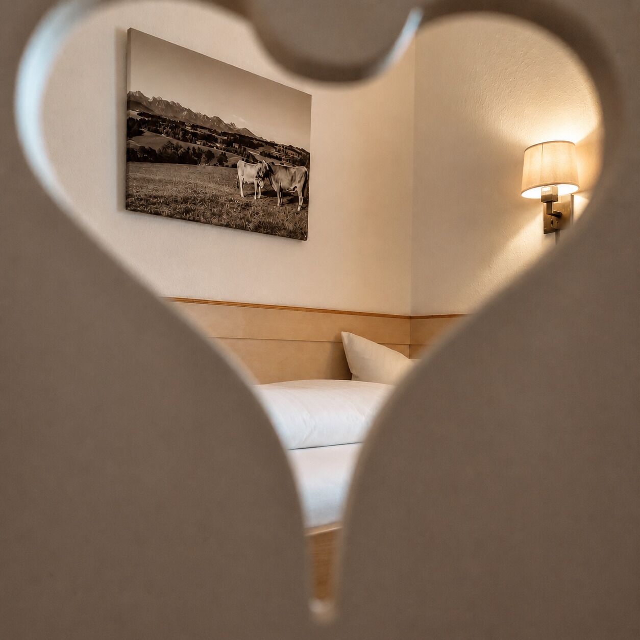Quarto com cama, luminária na parede e quadro de uma paisagem.