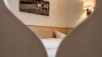Quarto com cama, luminária na parede e quadro de uma paisagem.