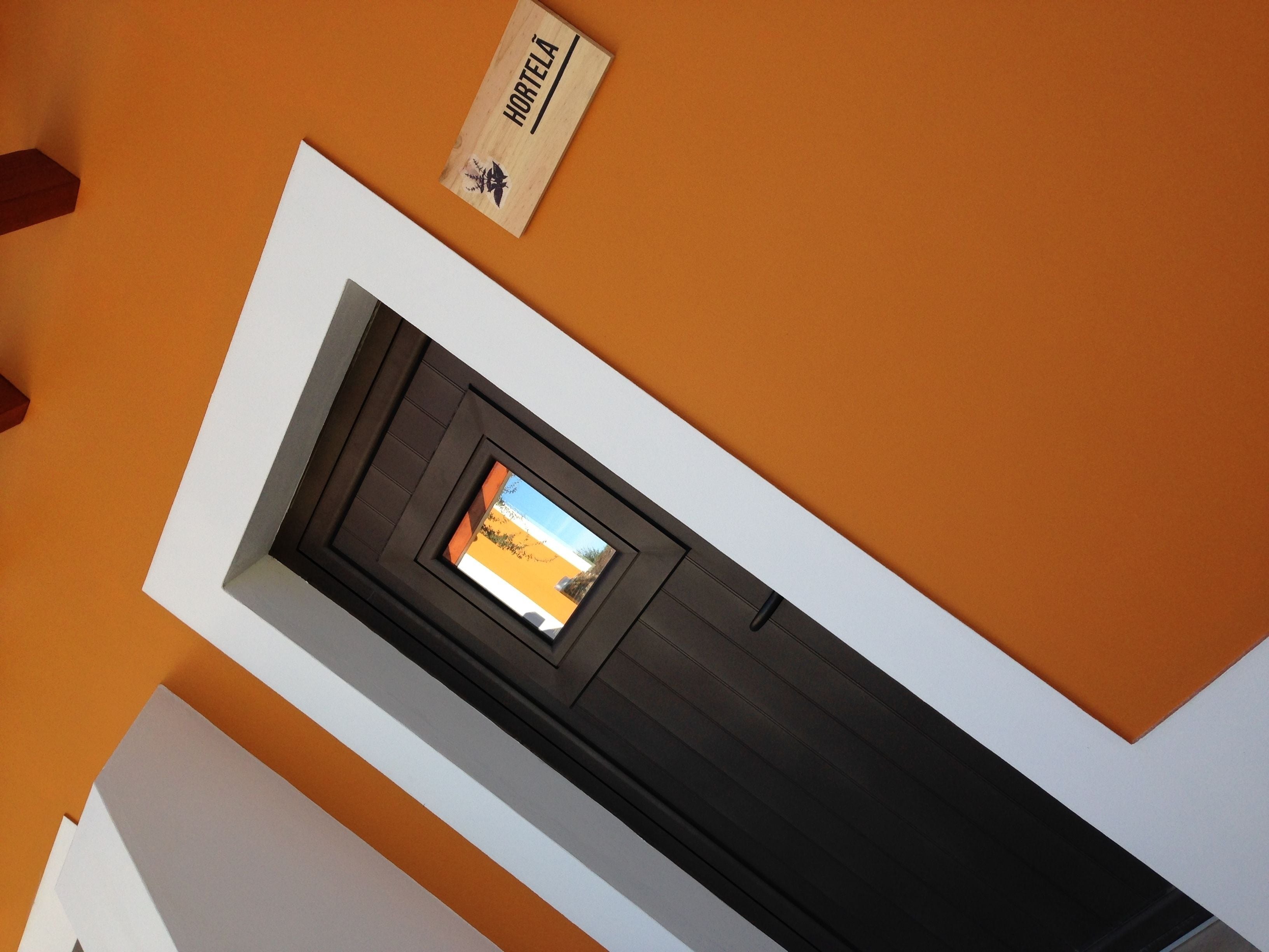 Interior de hotel com uma placa de madeira identificada como 'Hortelã' e uma moldura com uma paisagem cênica.