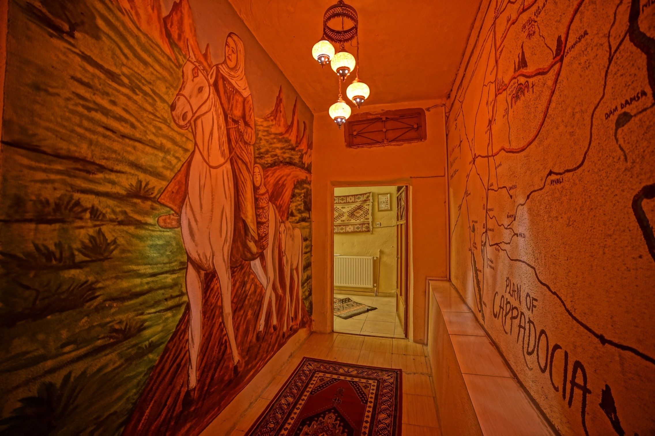 Um corredor com um mural de um cavaleiro e seu cavalo, um mapa na parede e um tapete estampado no chão.
