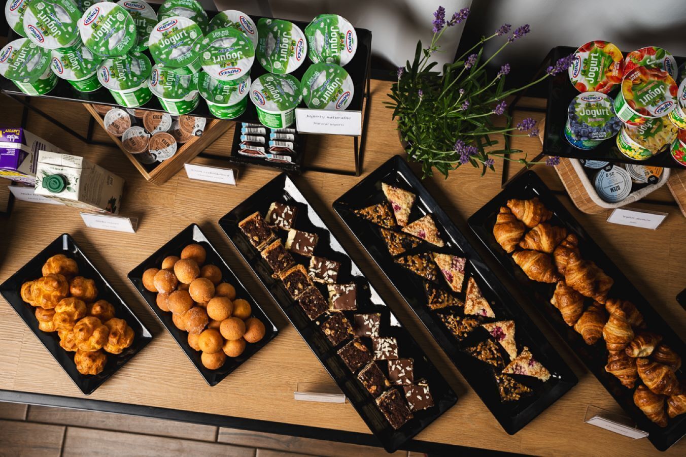 Diversos alimentos como iogurte, doces e sobremesas expostos em uma mesa de madeira.