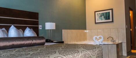 Quarto de hotel com uma cama grande, banheiro com banheira e um quadro emoldurado na parede.