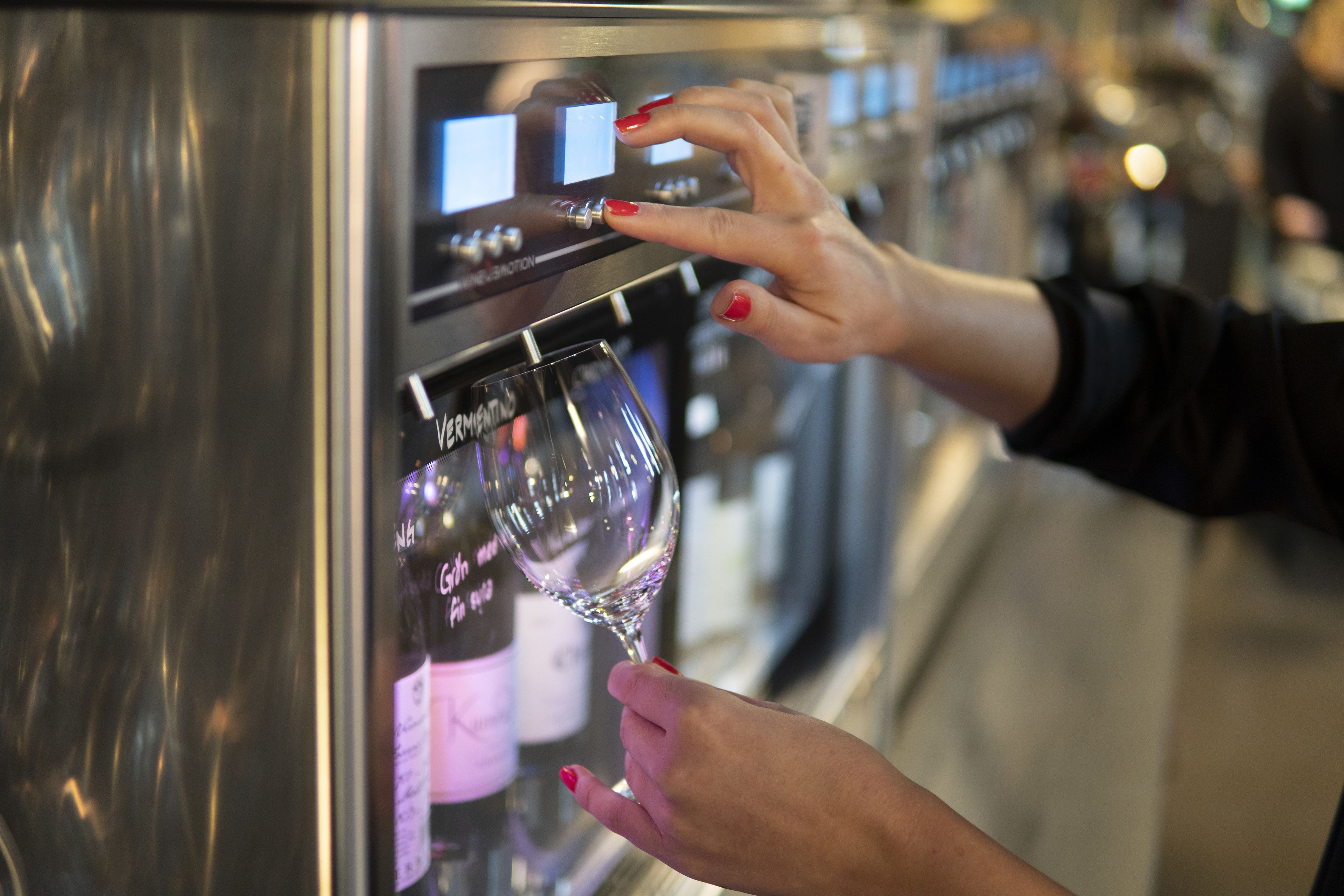 Uma pessoa utilizando uma máquina de dispensar vinho para servir num copo.