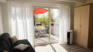 Quarto com sofá preto, porta de correr de vidro que dá para um pátio externo com mesa e cadeiras, e um armário branco.