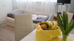 Quarto de hotel com cama, televisão, mesa de jantar com cesta de frutas e vaso com flores.