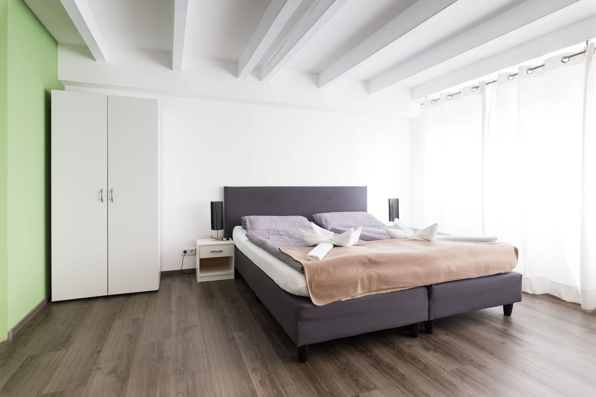 Quarto moderno com cama, mesa de cabeceira, guarda-roupa e uma janela grande com cortinas.