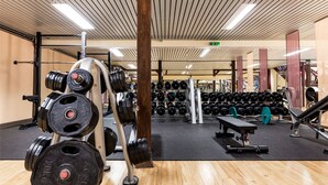 Academia com equipamento de musculação, piso de madeira e teto com padrões lineares.